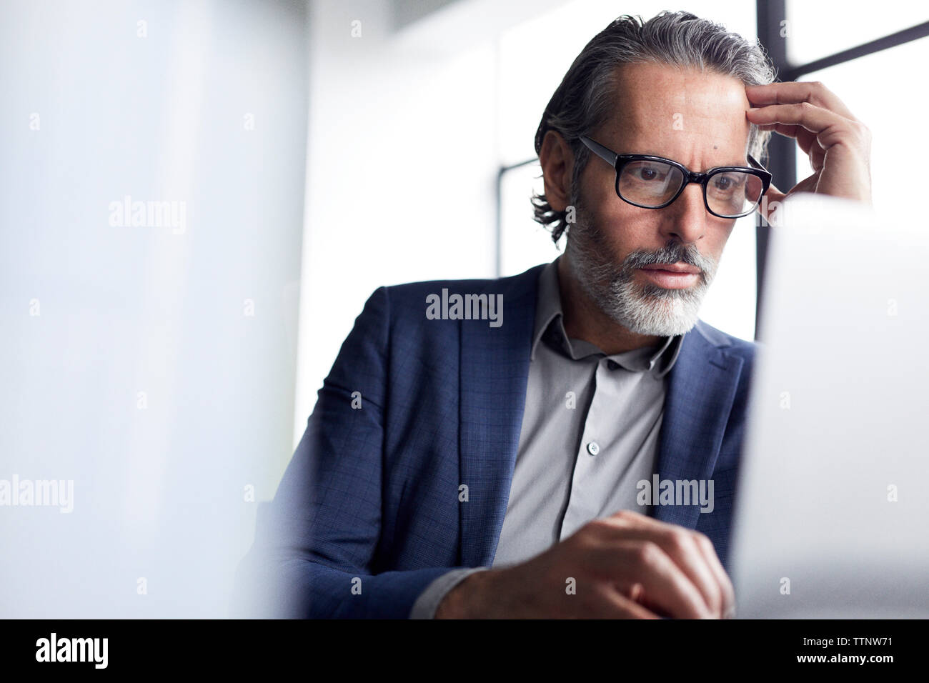 Serious businessman with head in hand using laptop computer while ...