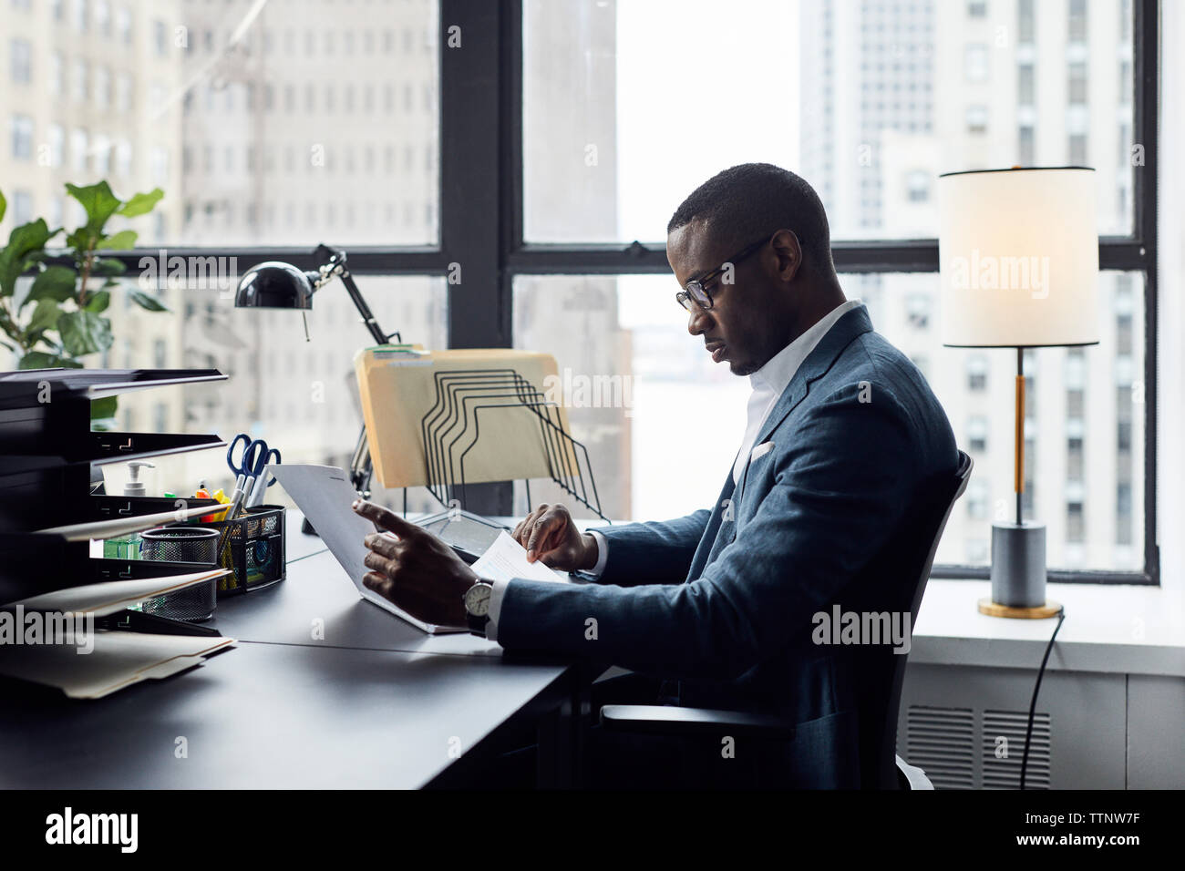 Serious businessman working while sitting against window in office ...