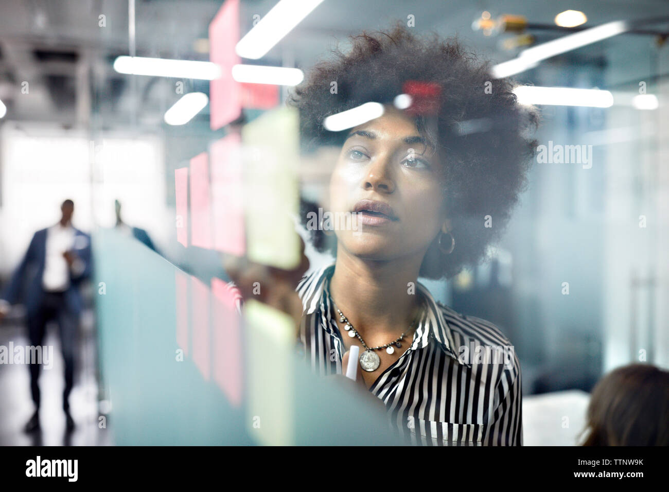 Focused businesswoman looking at adhesive notes seen through window in ...