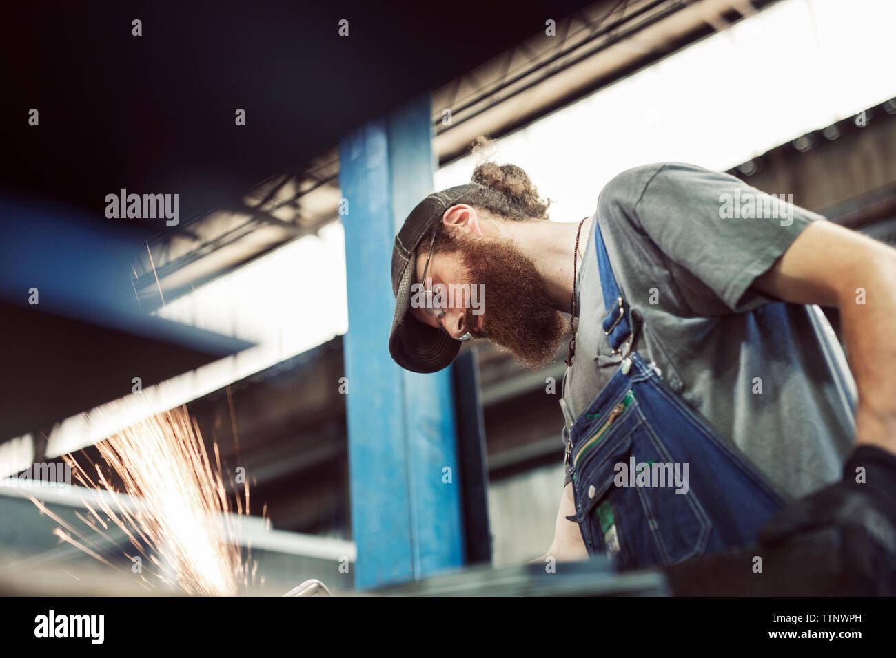 Low angle view of blue collar worker using welding machine in steel ...