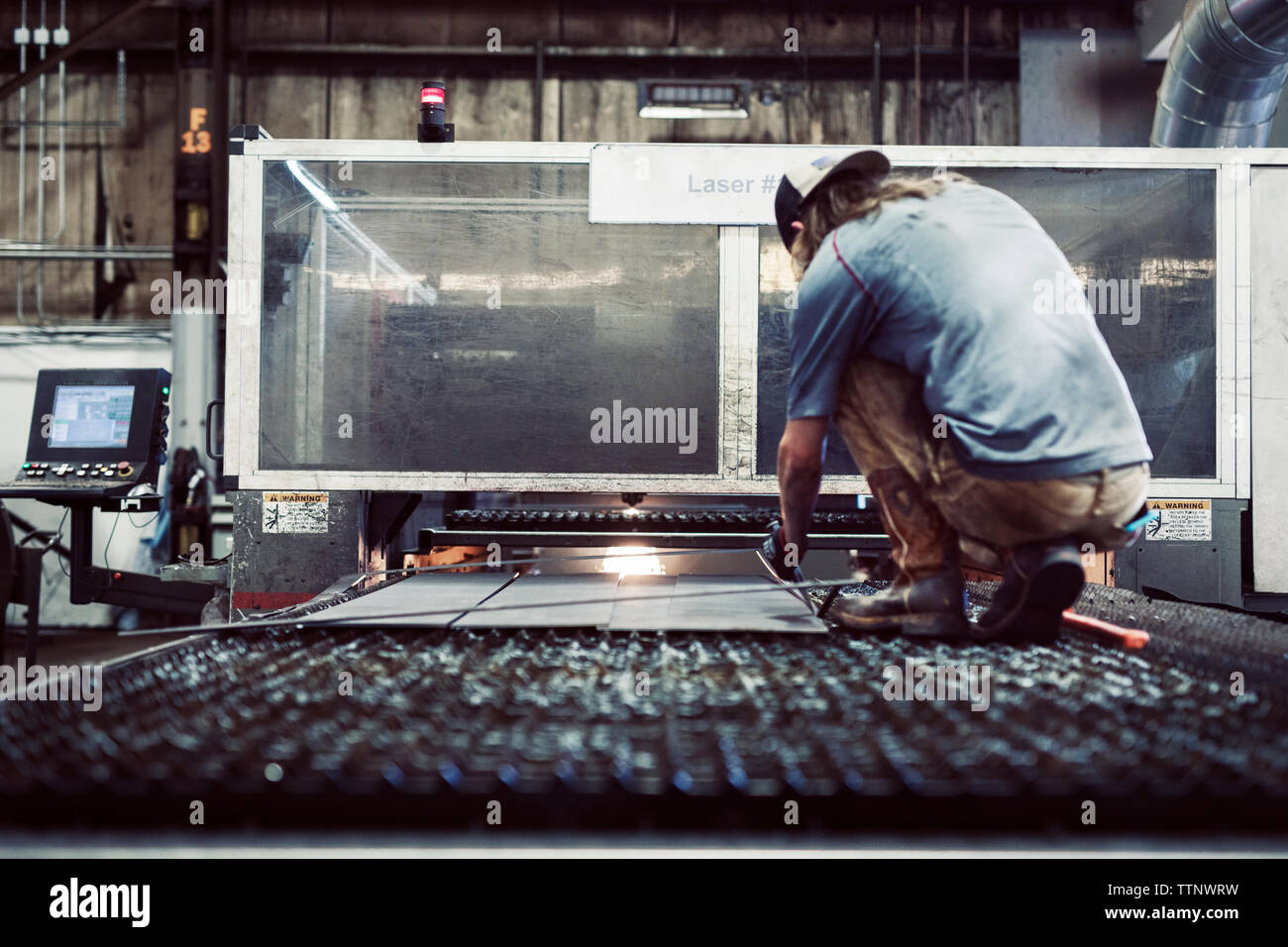 Full length of worker crouching while working on steel sheets at ...