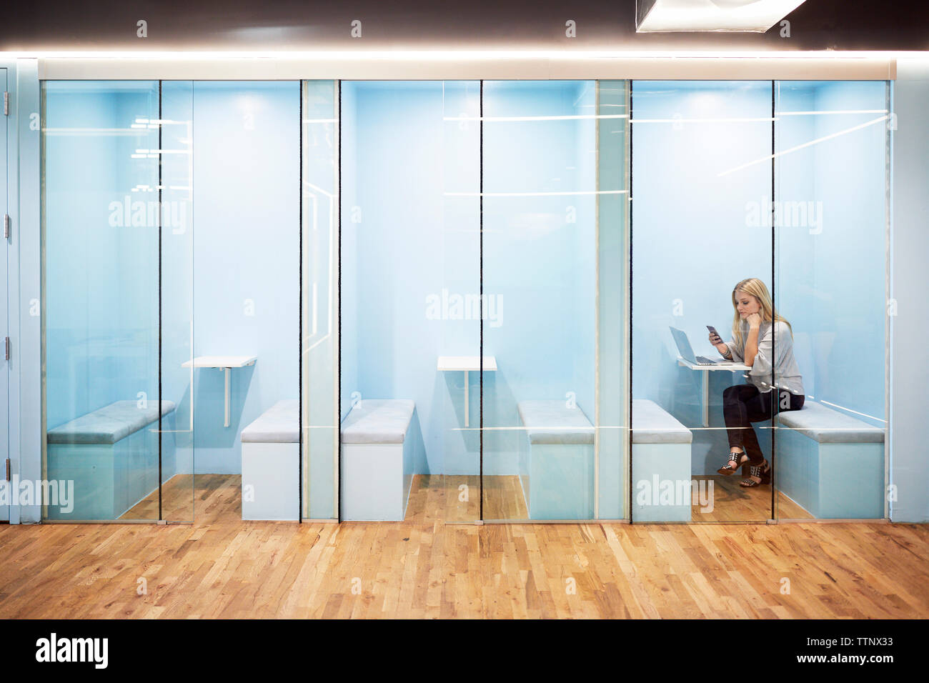 businesswoman using laptop and mobile phone while sitting in cubicle at ...