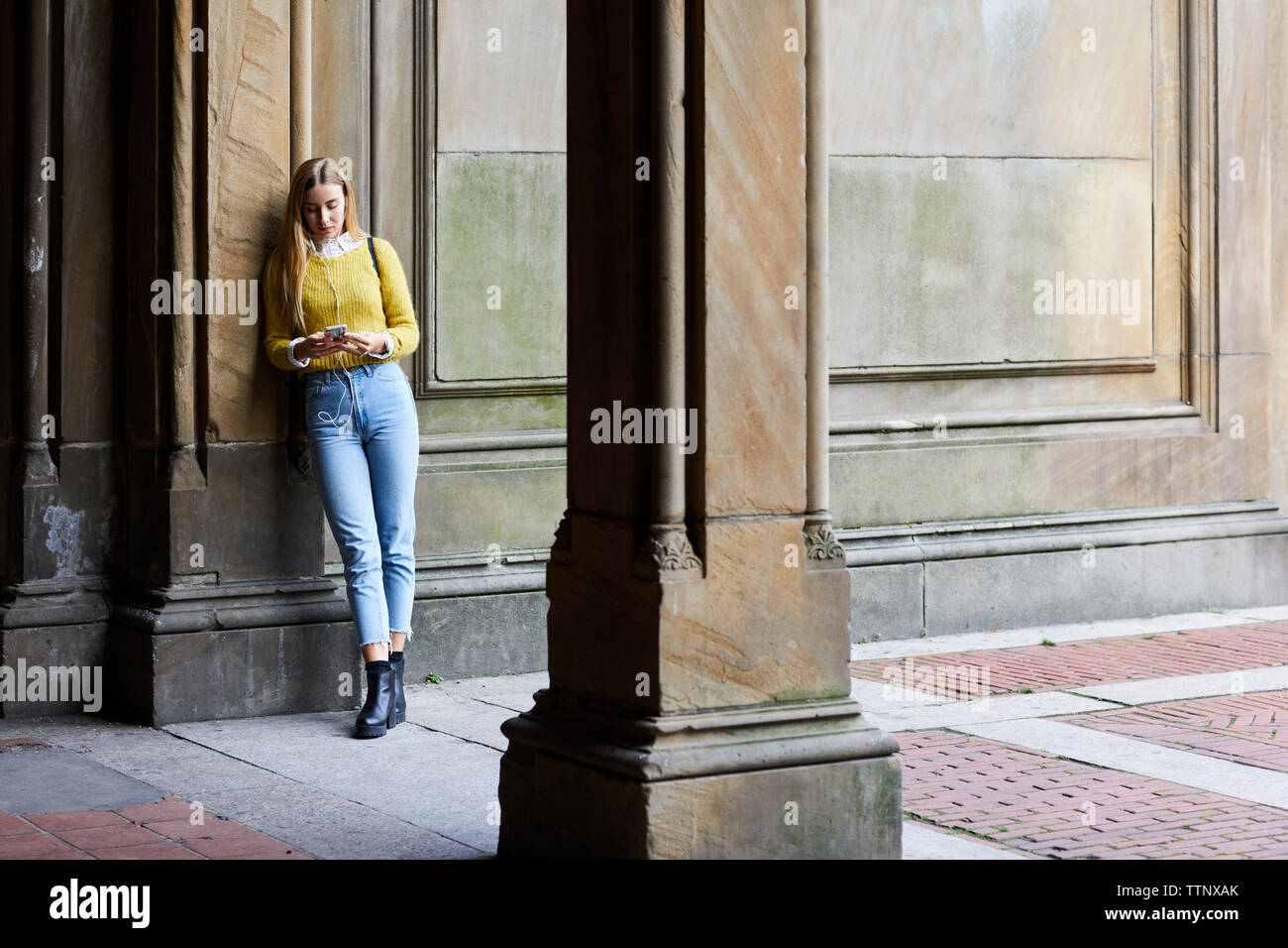 Full length of woman using mobile phone while standing by wall Stock ...