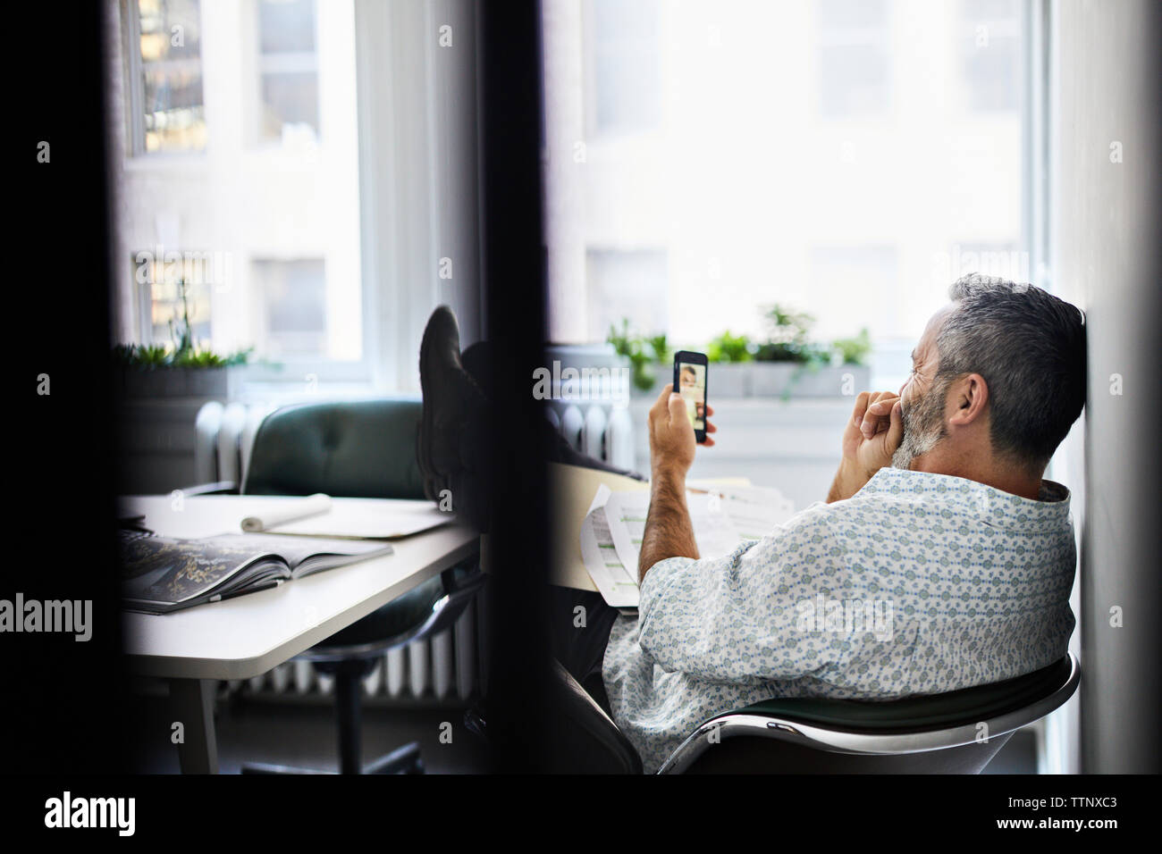 businessman using smart phone with feet up at conference table in board ...