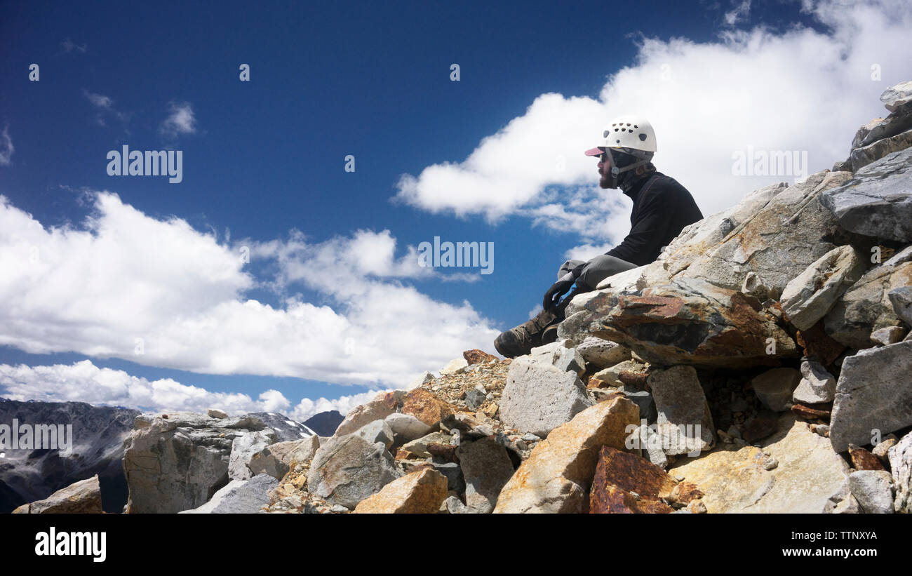 Side view of man sitting on rock against sky Stock Photo - Alamy