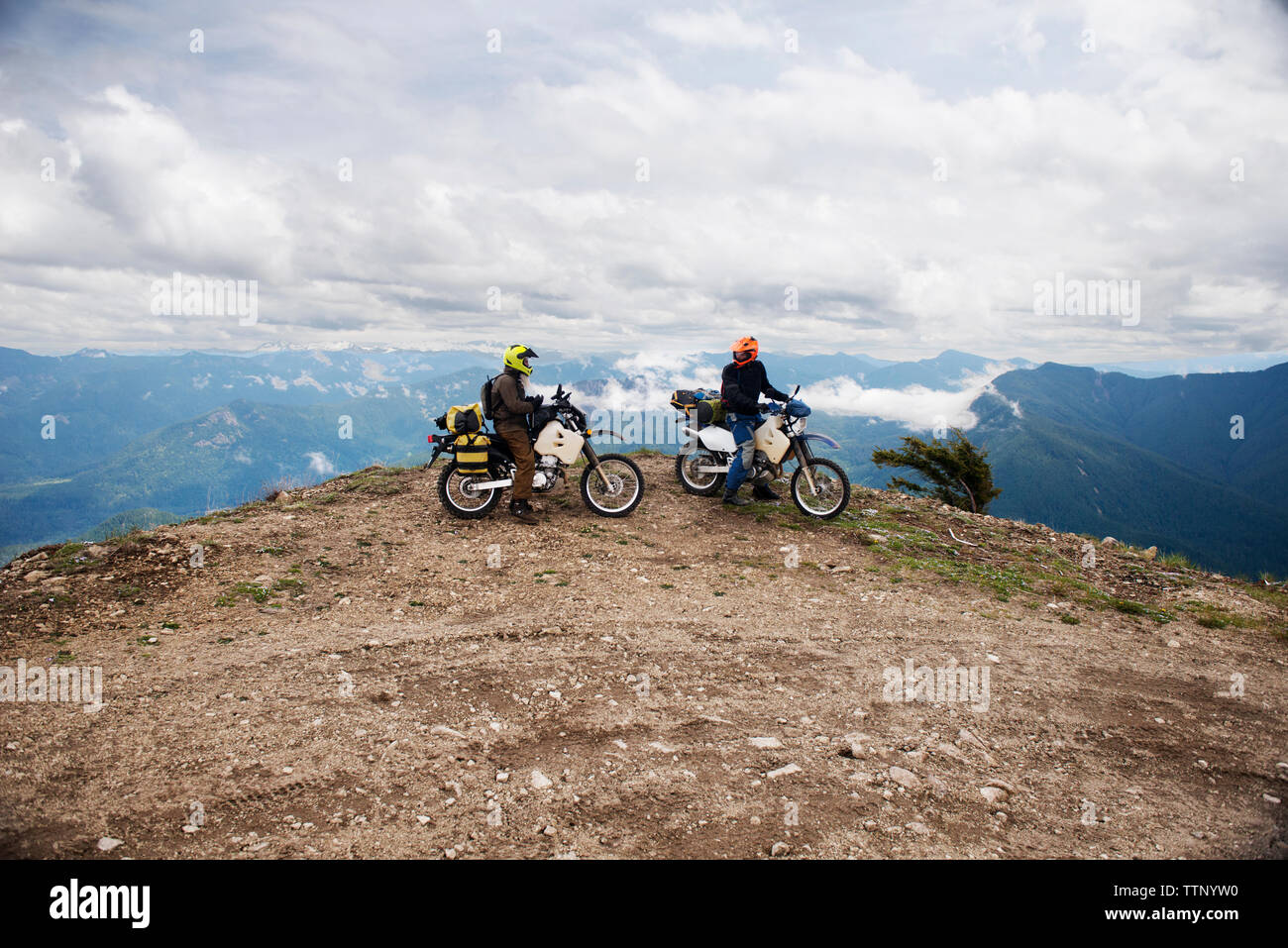 Friends riding motorcycle on cliff against cloudy sky Stock Photo - Alamy