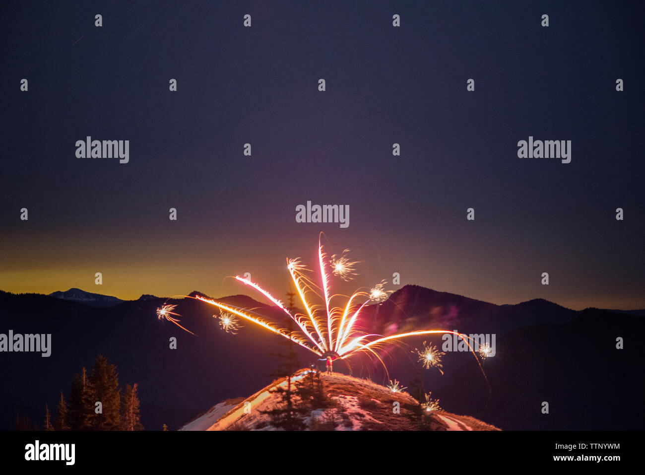 Firework display on hill against silhouette mountain range during ...