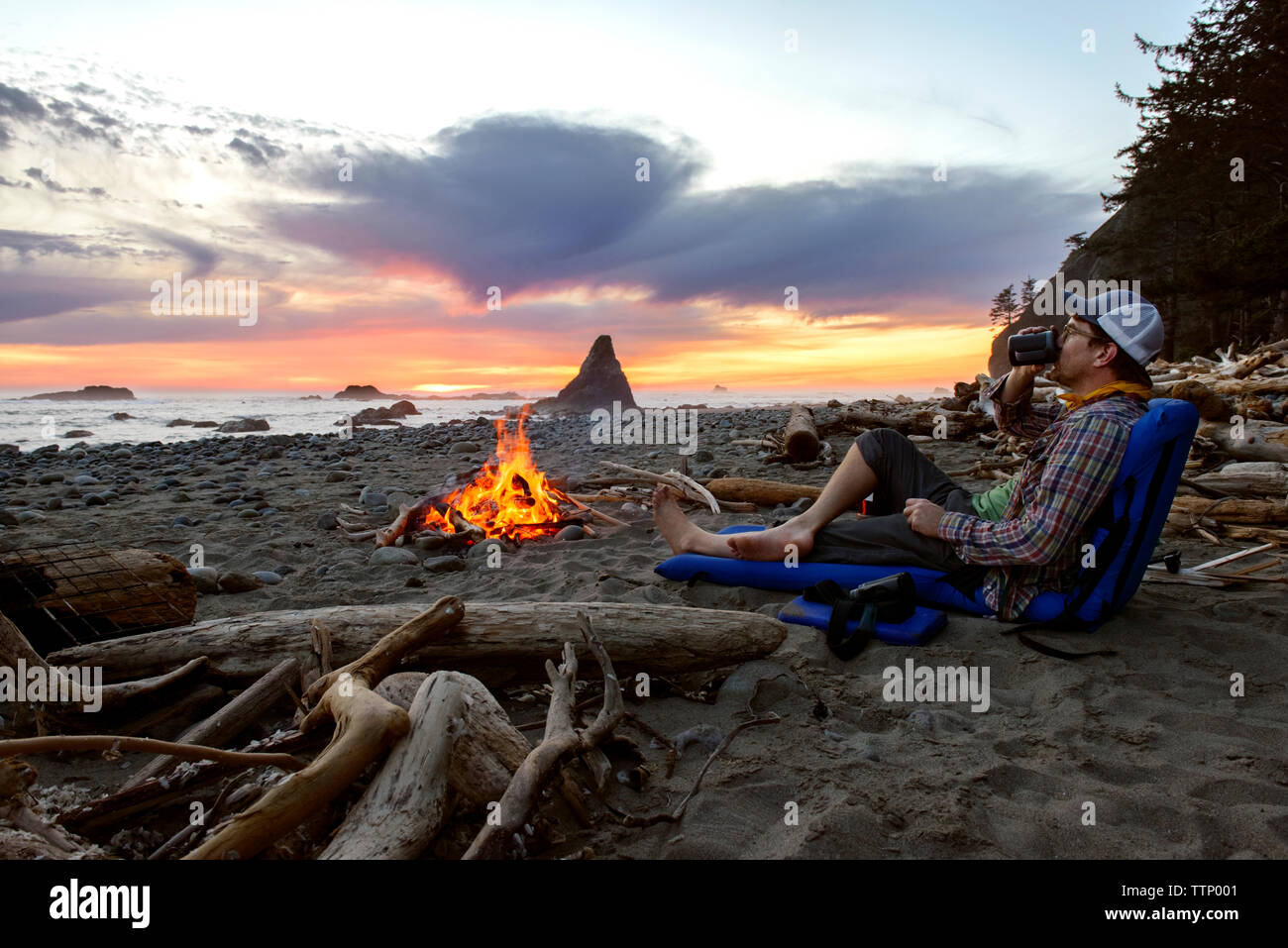 Man relaxing by campfire at seashore during sunset Stock Photo - Alamy