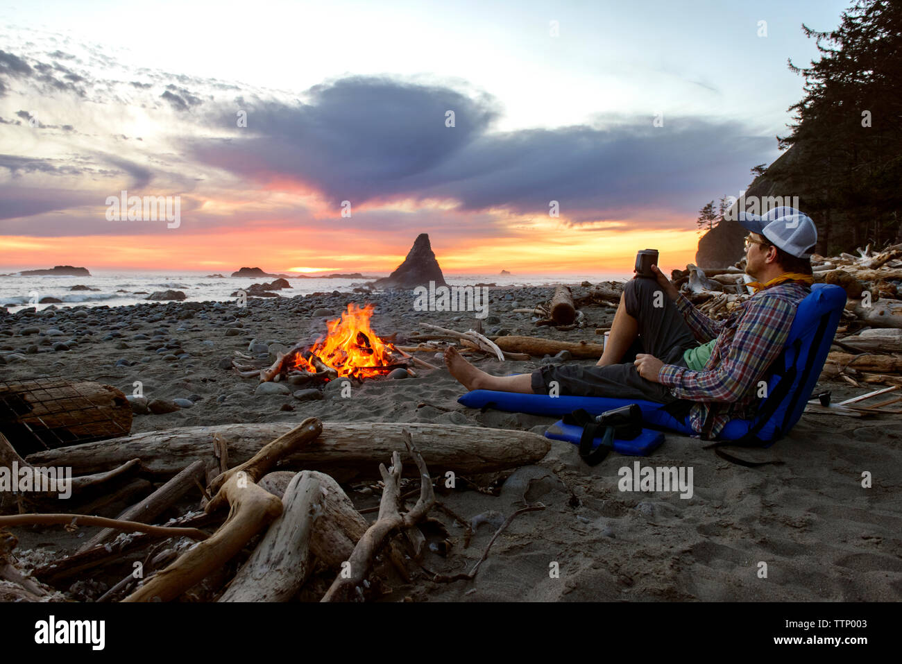 Man sitting by campfire at seashore Stock Photo - Alamy