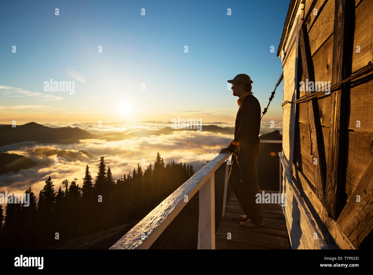 Side view of man looking at mountain view from log cabin during sunset ...