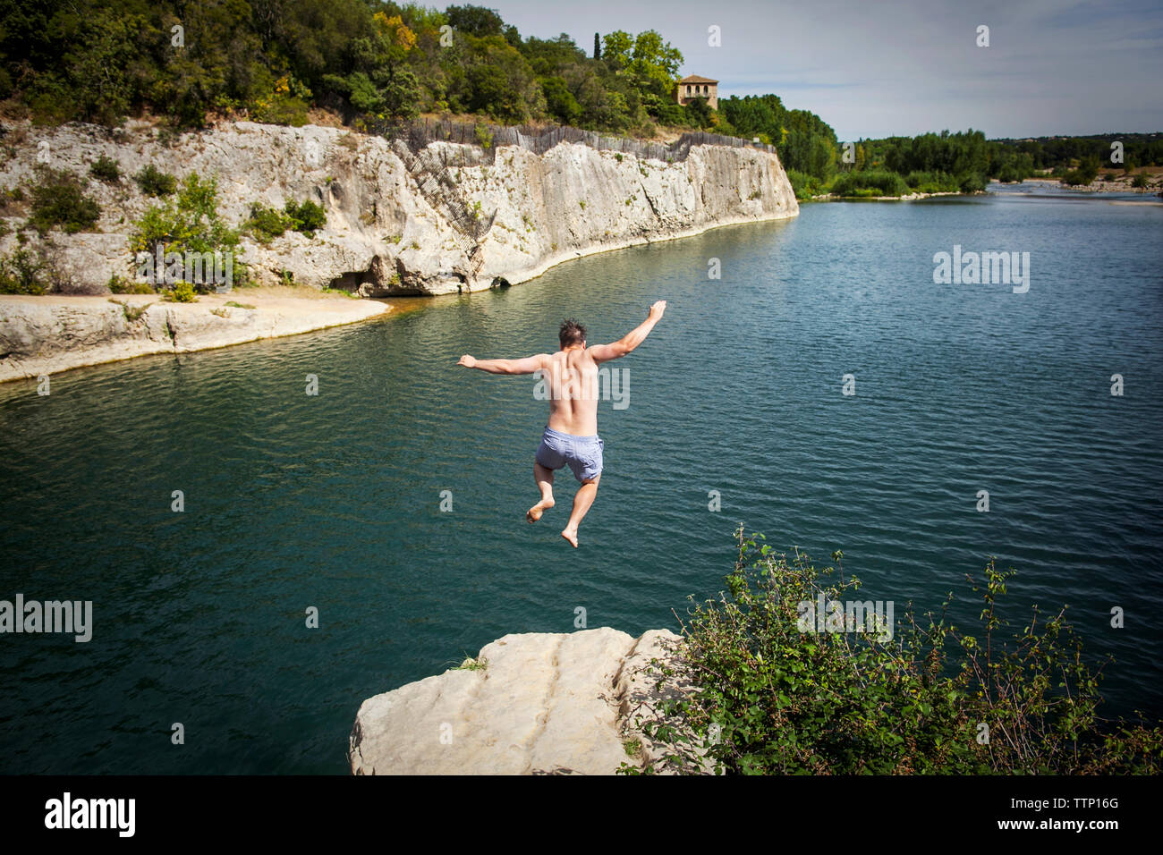 Rear view of man diving off rock into river Stock Photo - Alamy