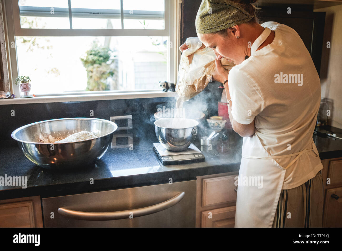 Concentrated woman pouring powder in container while standing at ...