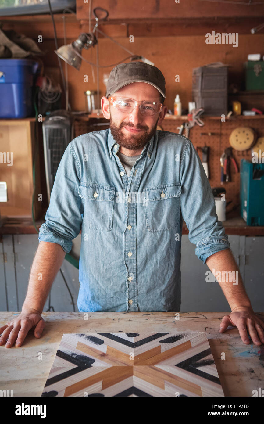 Portrait of smiling craftsperson with wooden art at workbench Stock ...