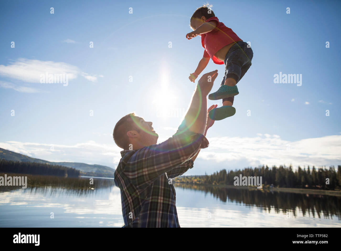 Side view of playful father throwing son in air against lake and sky ...