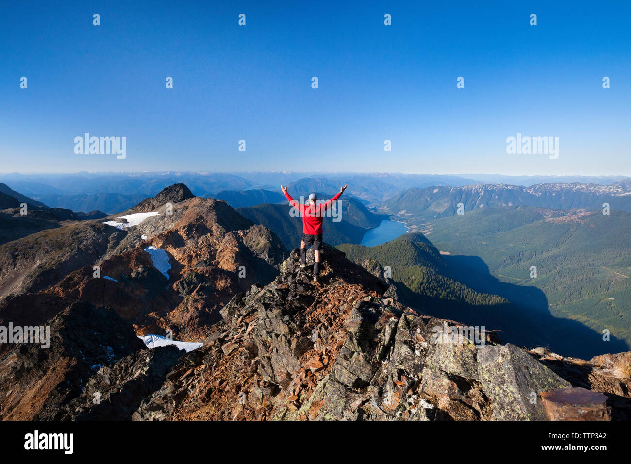 Rear view of hiker with arms raised standing on mountain against clear ...