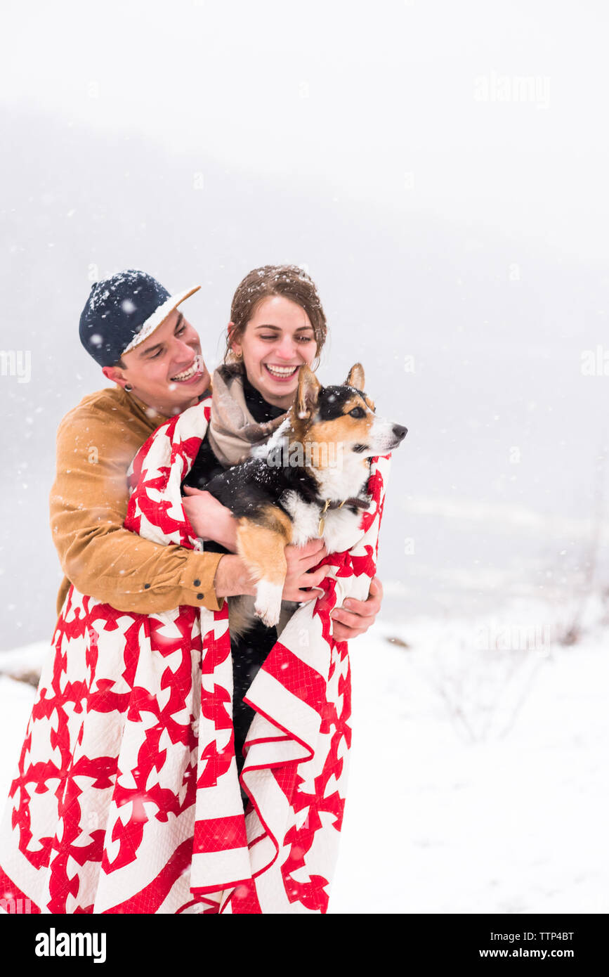 Young couple laugh and huddle during snowfall with dog Stock Photo - Alamy