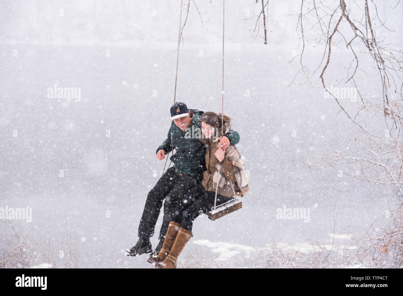 Couple laughing on swing over river during snowfall Stock Photo - Alamy