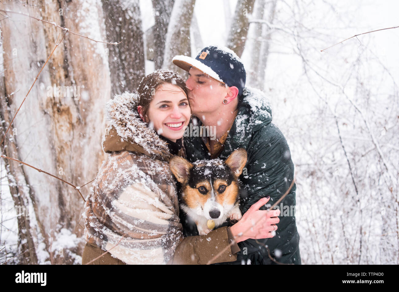 Couple huddled together with dog in forest during snowfall Stock Photo ...