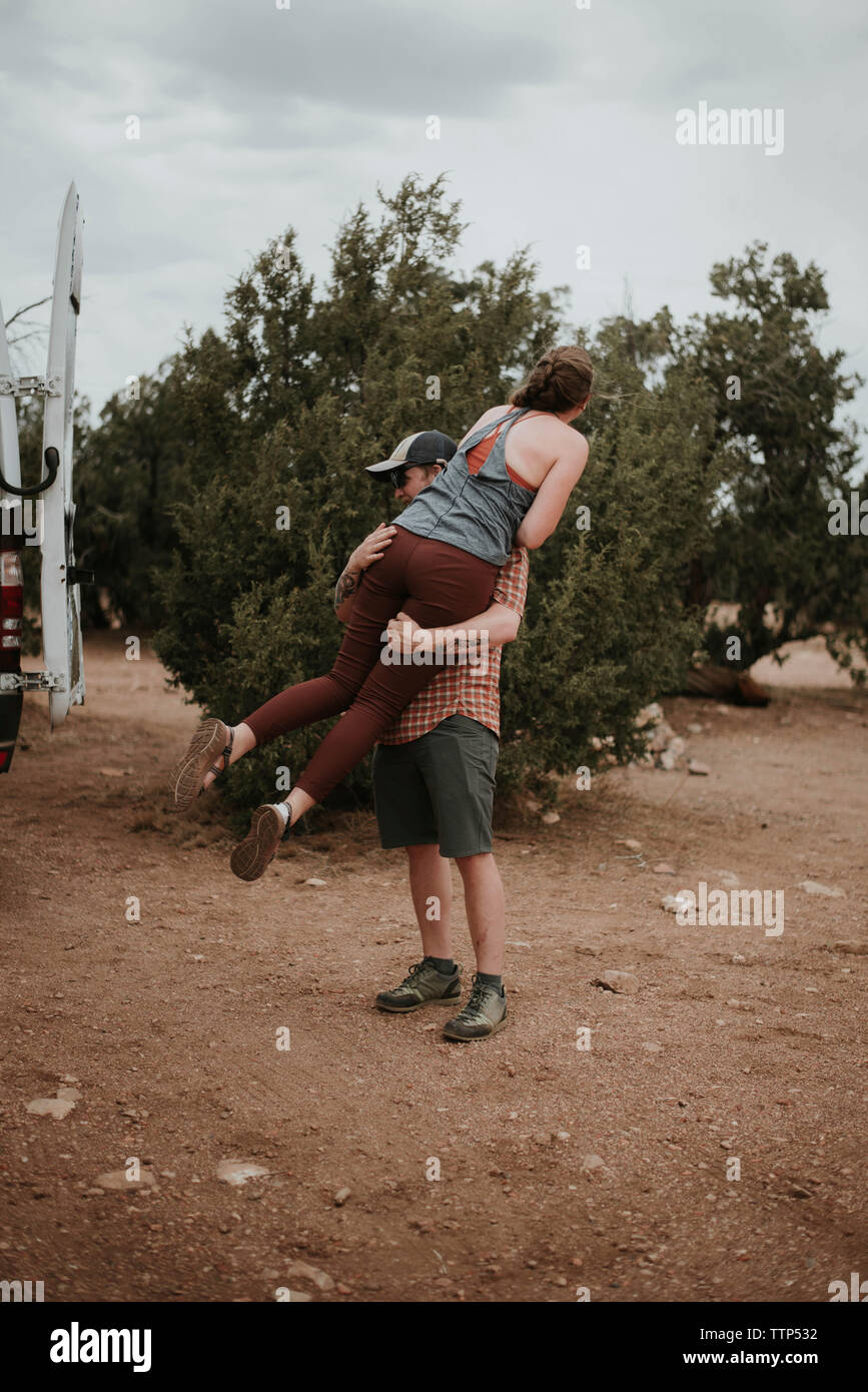 Happy boyfriend carrying girlfriend while standing on field against ...