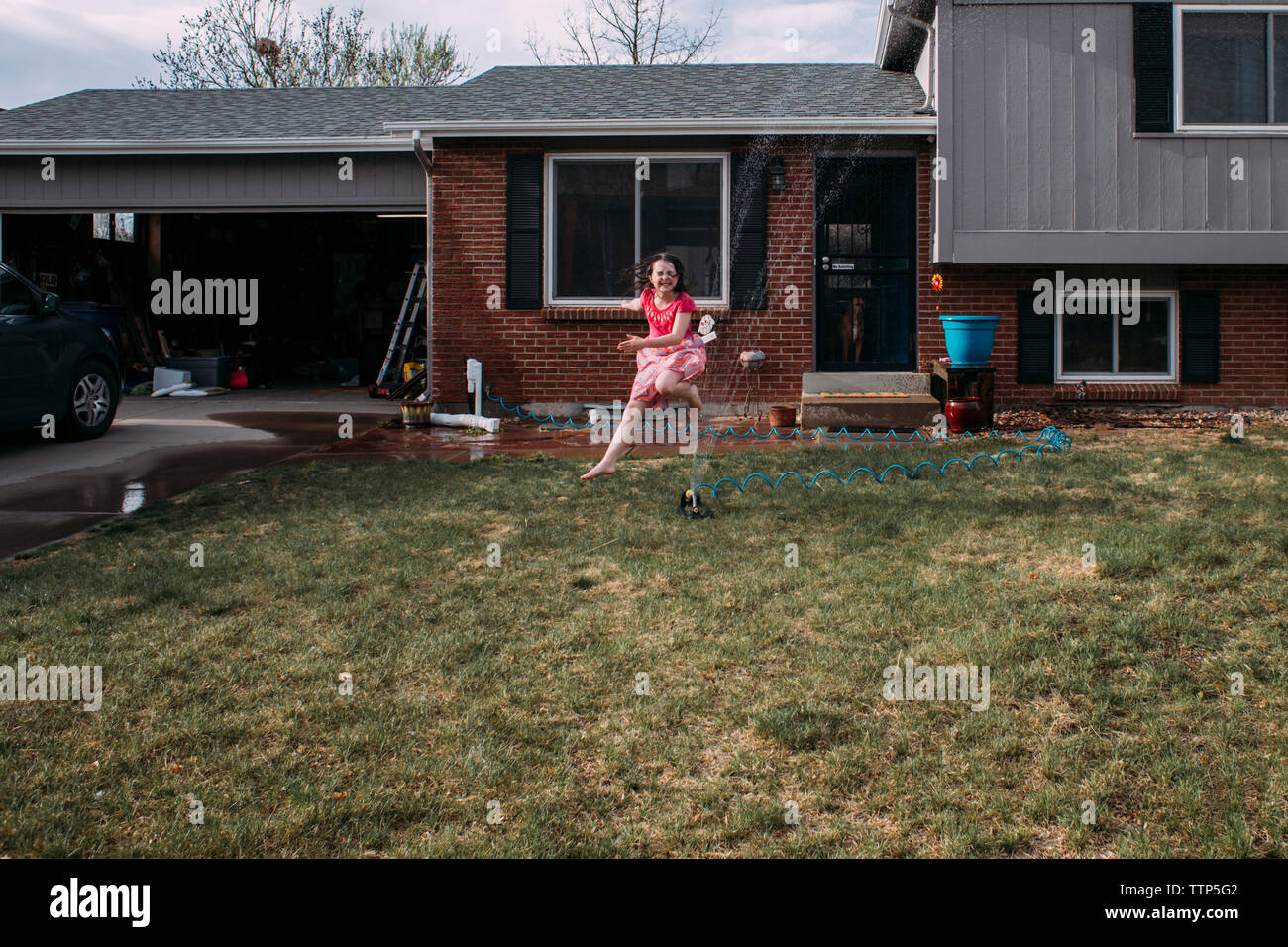 Playful girl running at yard in sprinkler against house Stock Photo - Alamy