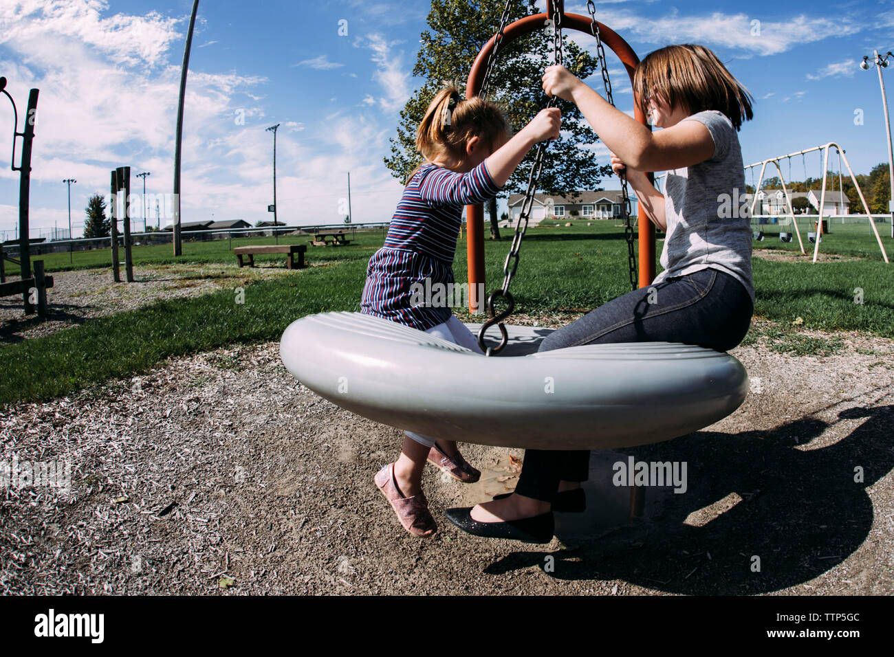 Sisters playing on swing at playground during sunny day Stock Photo - Alamy
