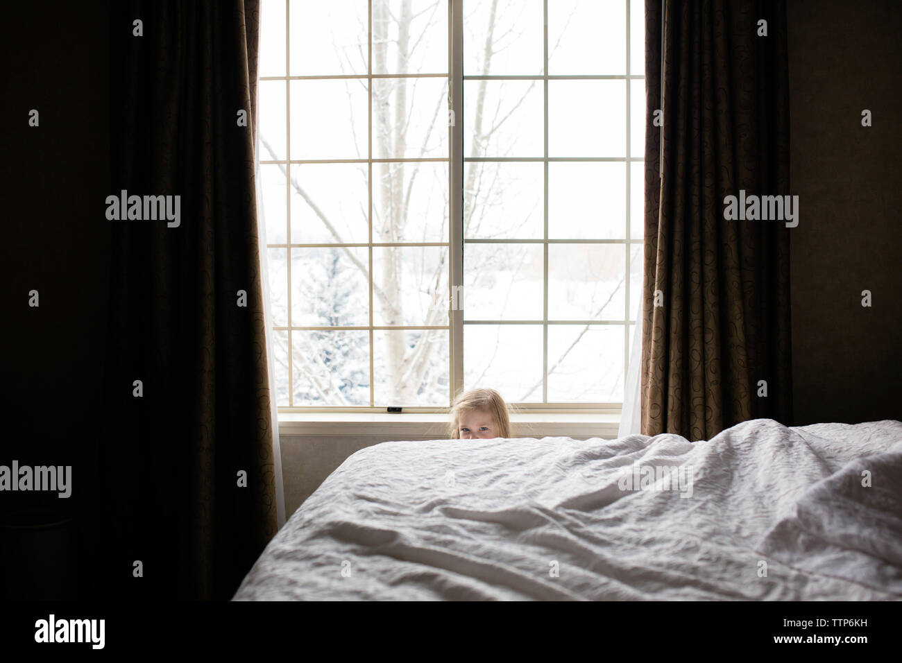 Portrait of girl hiding behind bed at home Stock Photo - Alamy