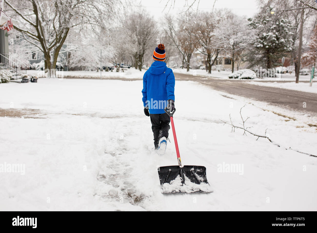 Boy dragging shovel through snow outside Stock Photo - Alamy