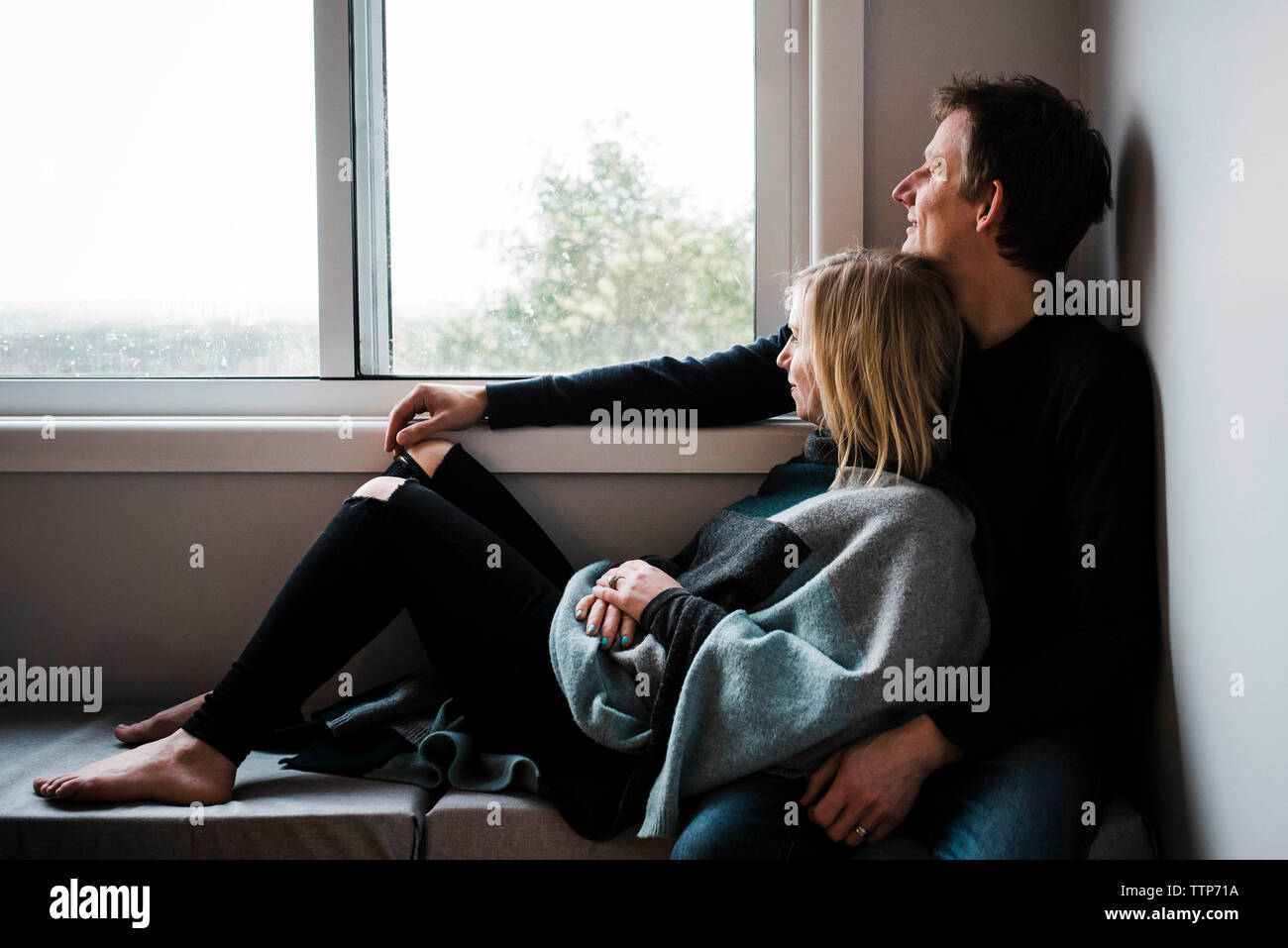 Thoughtful loving couple looking through window while resting at home ...
