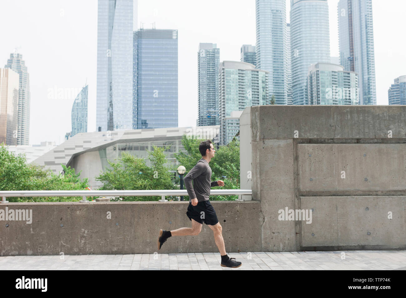 Side view of man running on footbridge against modern buildings in city ...