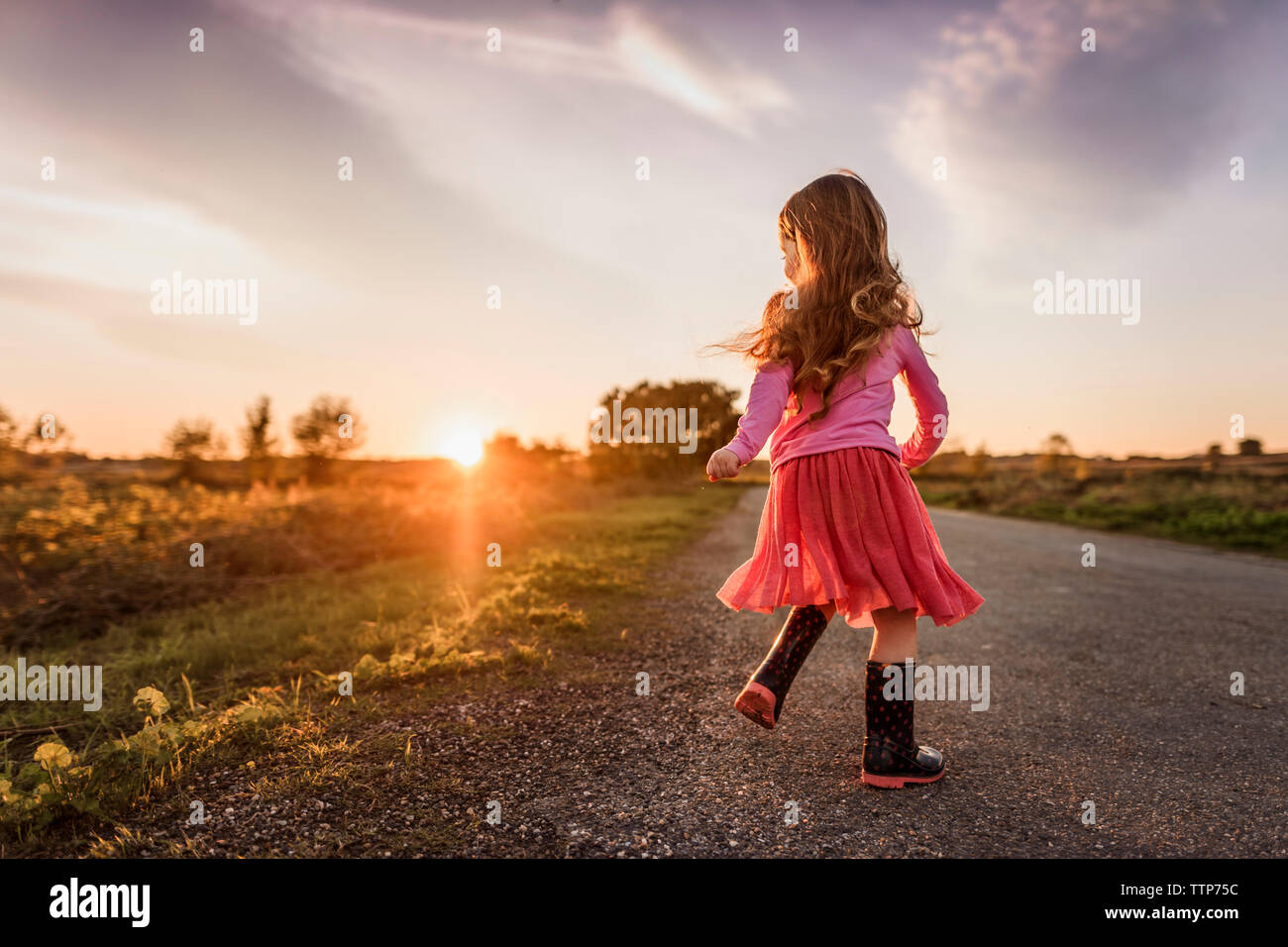 girl plays in evening sun twirling on road with backlight Stock Photo ...