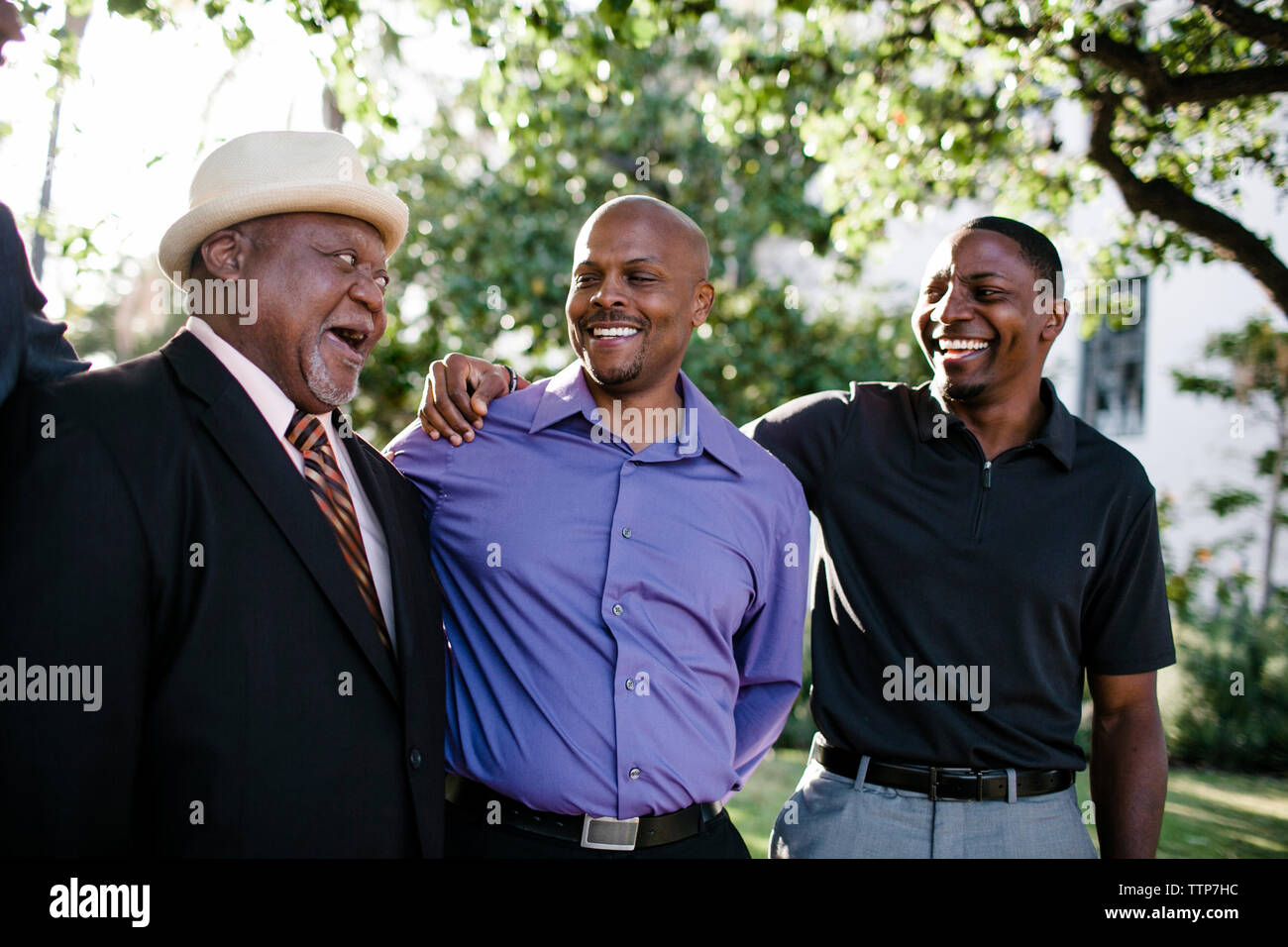 Happy father talking with sons while standing against trees at park ...