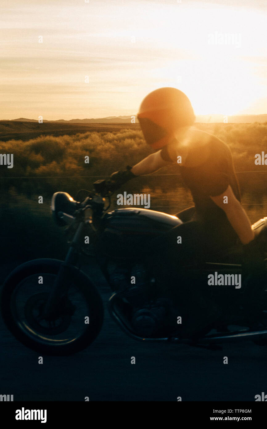 Side view of man riding motorcycle on street during sunset Stock Photo ...