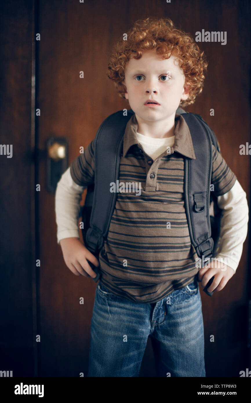 Curious boy carrying backpack while standing against door Stock Photo ...