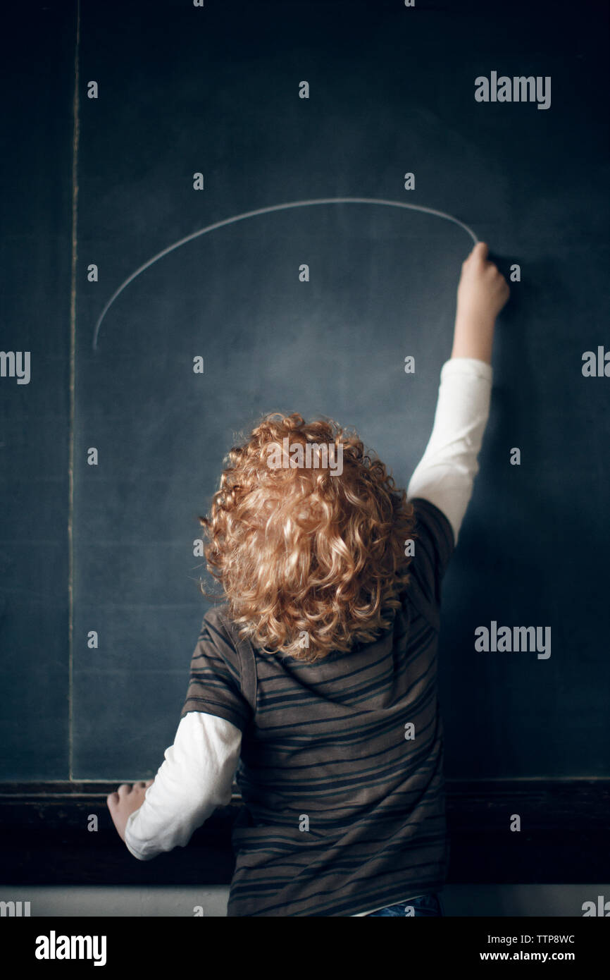 Rear view of schoolboy drawing on blackboard Stock Photo - Alamy