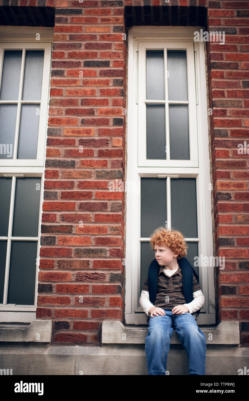 Boy sitting against window of school building Stock Photo - Alamy