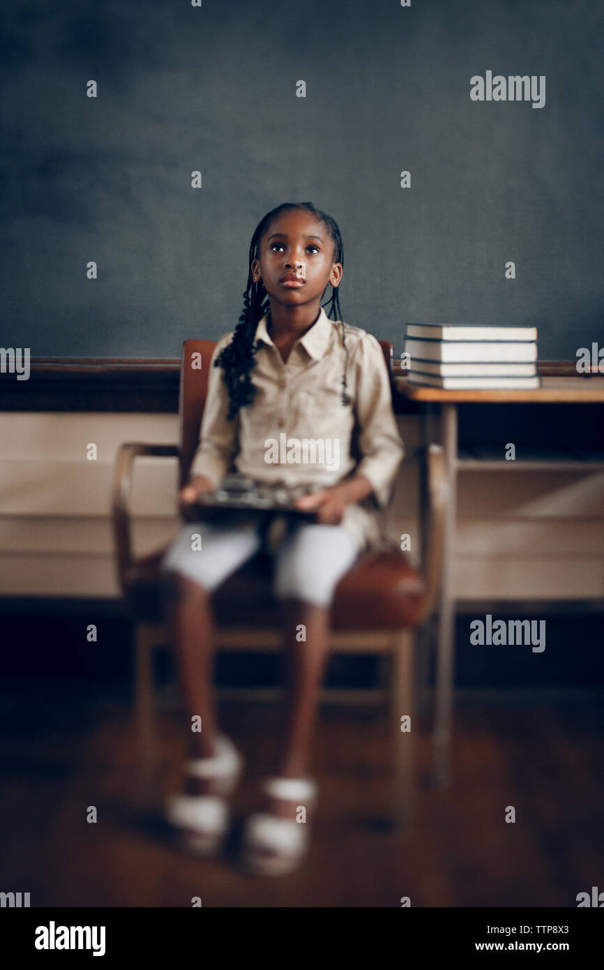 Girl sitting with books by table against blackboard in classroom Stock ...