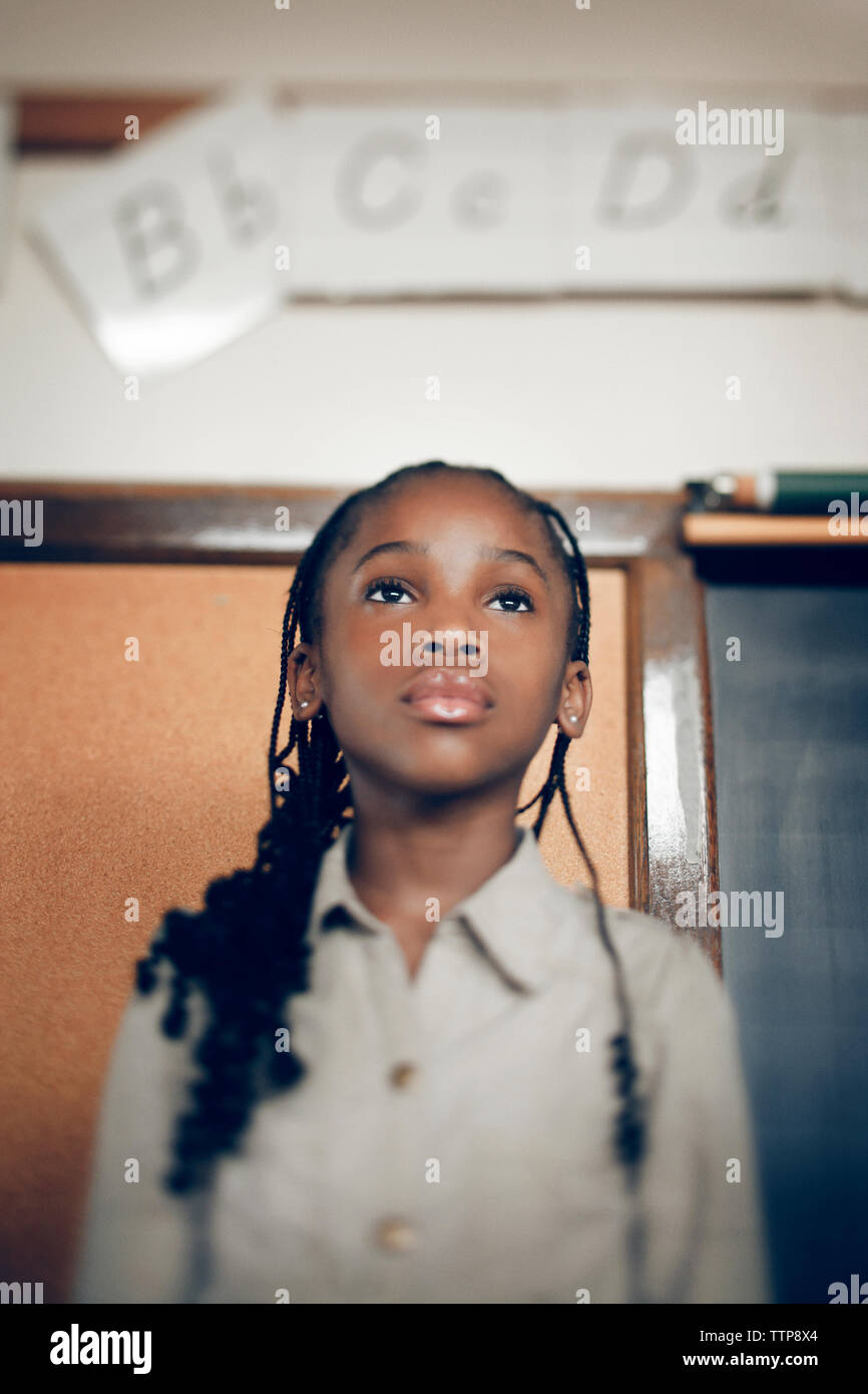 Close-up of thoughtful girl standing against blackboard in classroom ...