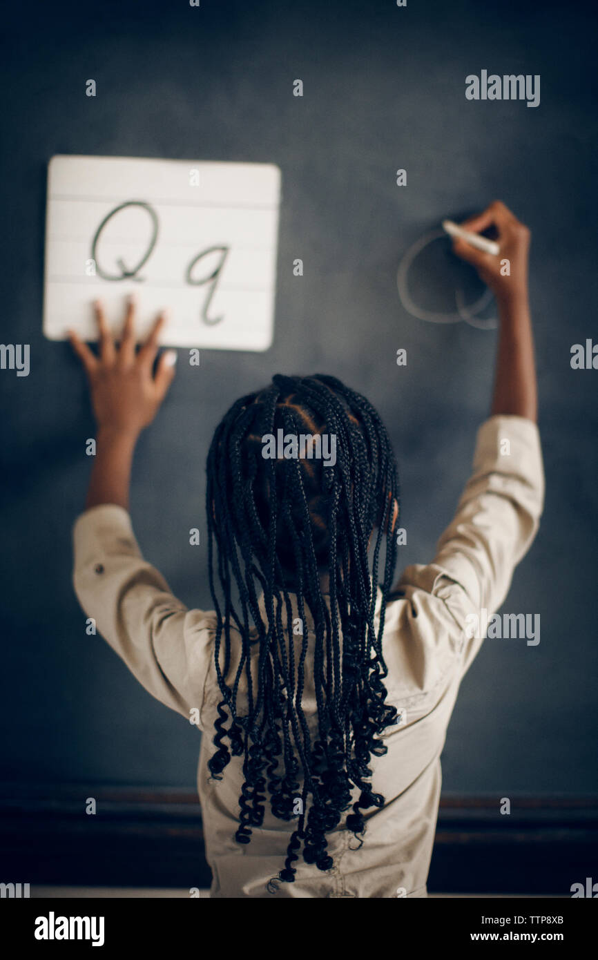 Rear view of schoolgirl with braided hair writing alphabet Q on ...