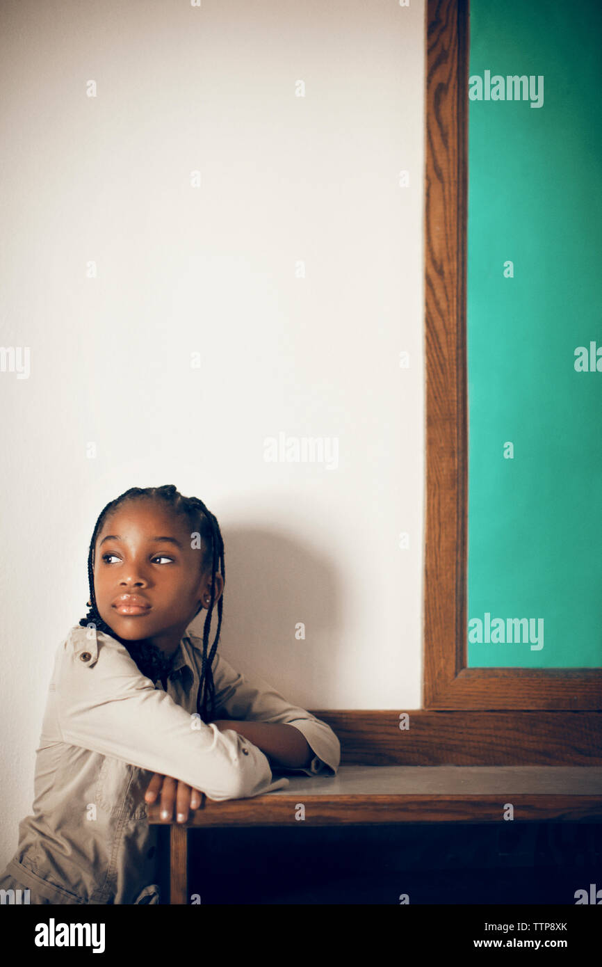 Side view of thoughtful girl sitting by blackboard in classroom Stock ...