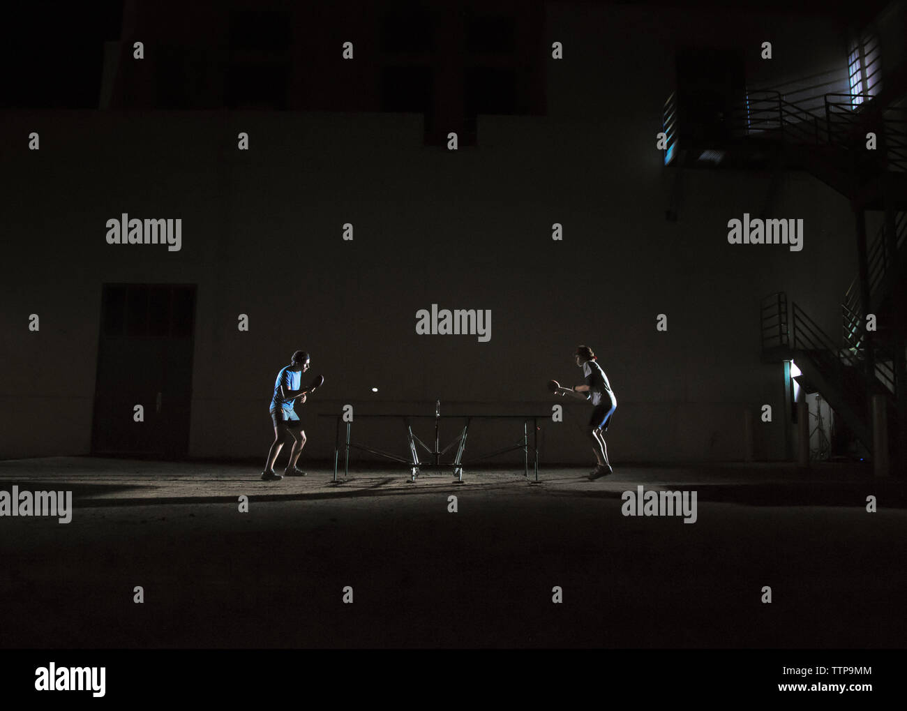 Friends playing table tennis against building at night Stock Photo - Alamy