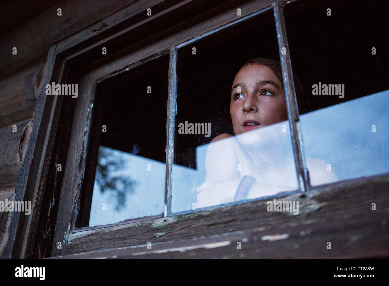 Low angle view of thoughtful girl looking through window seen through ...