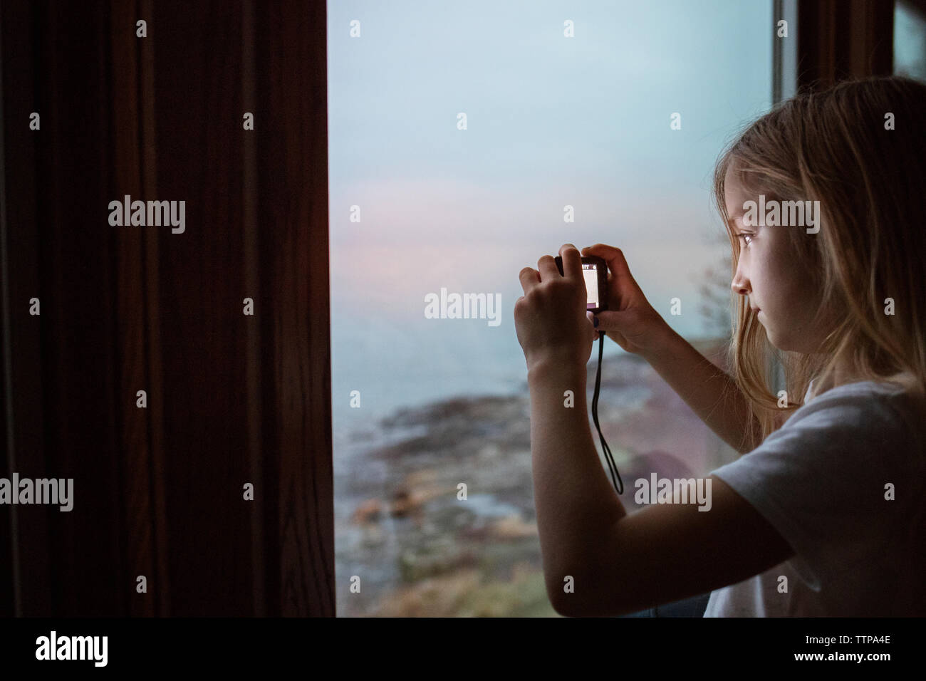 Side view of girl photographing through window while standing in log ...