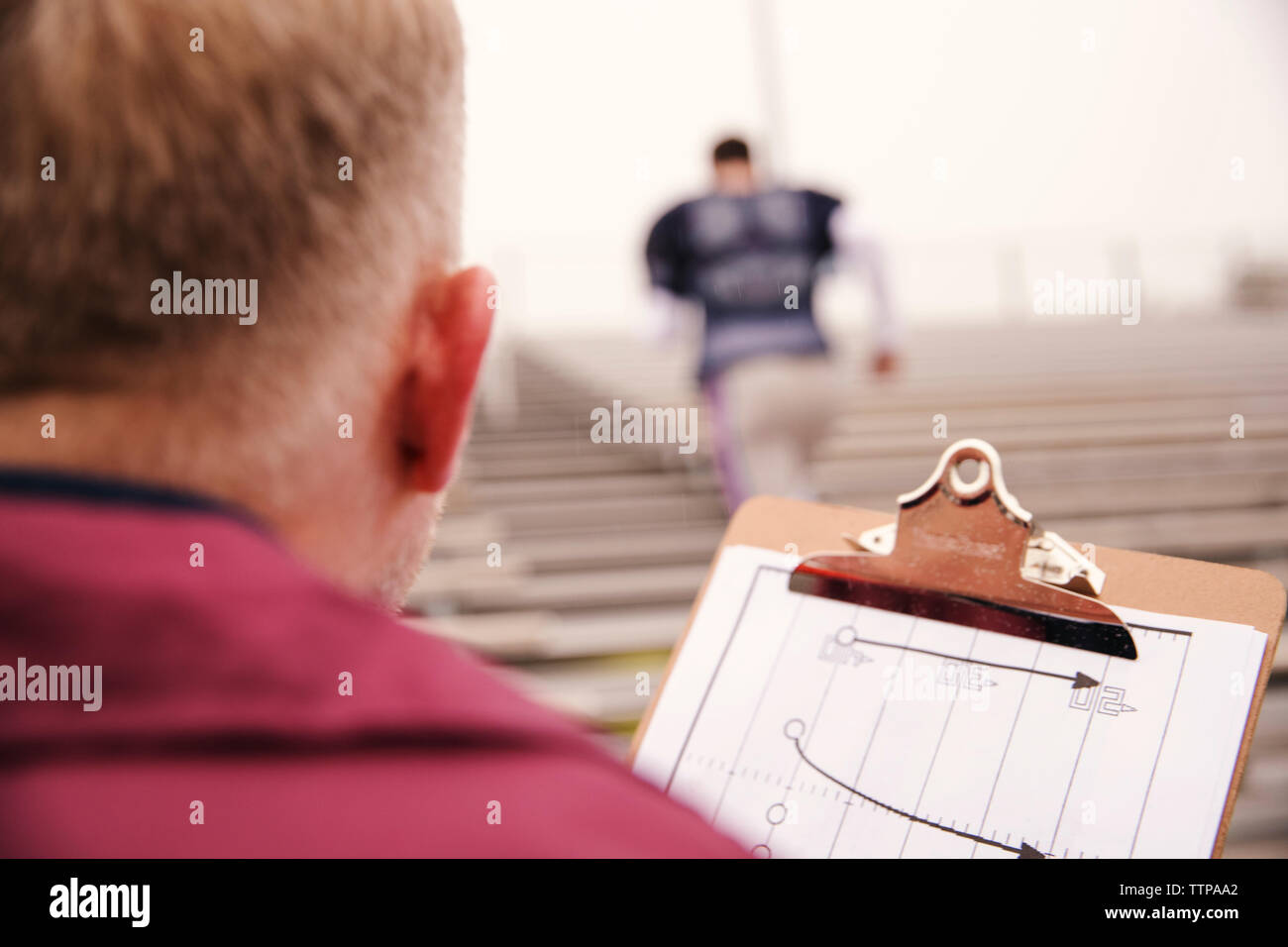Rear view of coach holding clipboard looking at American football ...