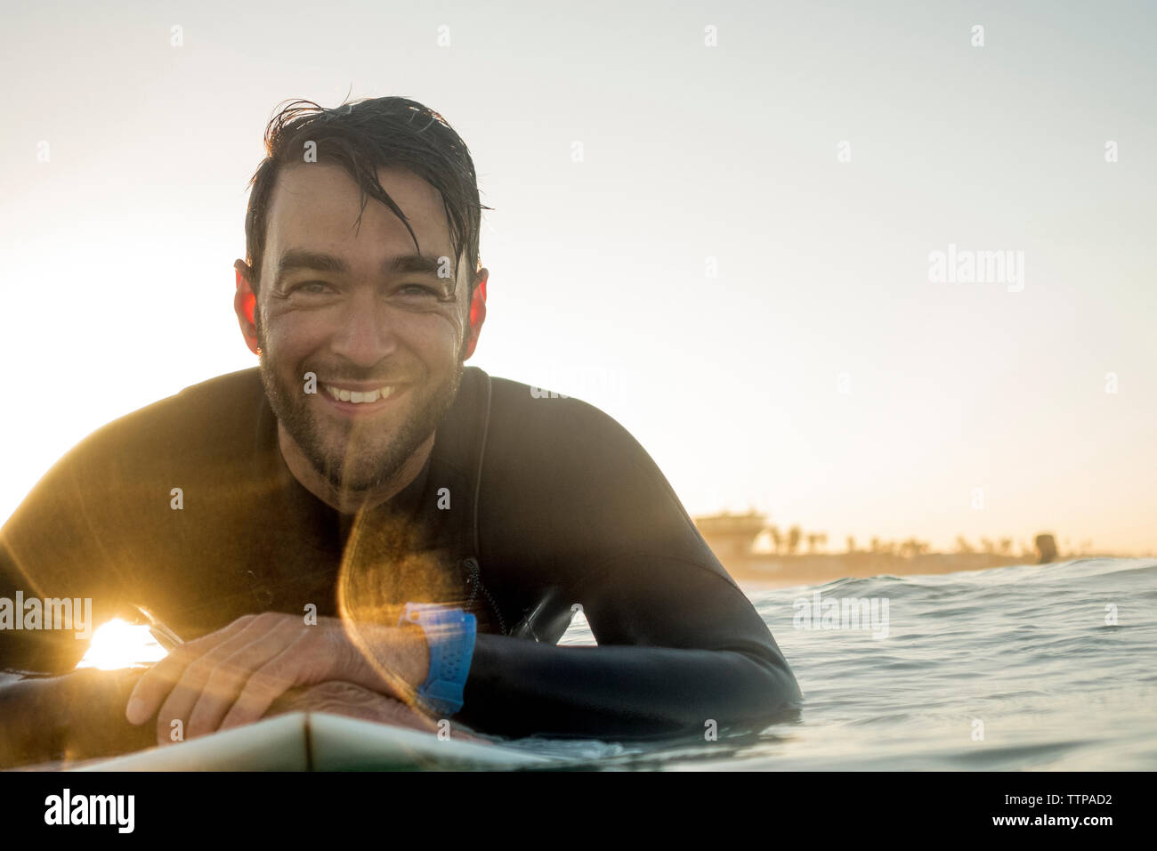 Portrait of happy male surfer lying on surfboard in sea during sunset ...