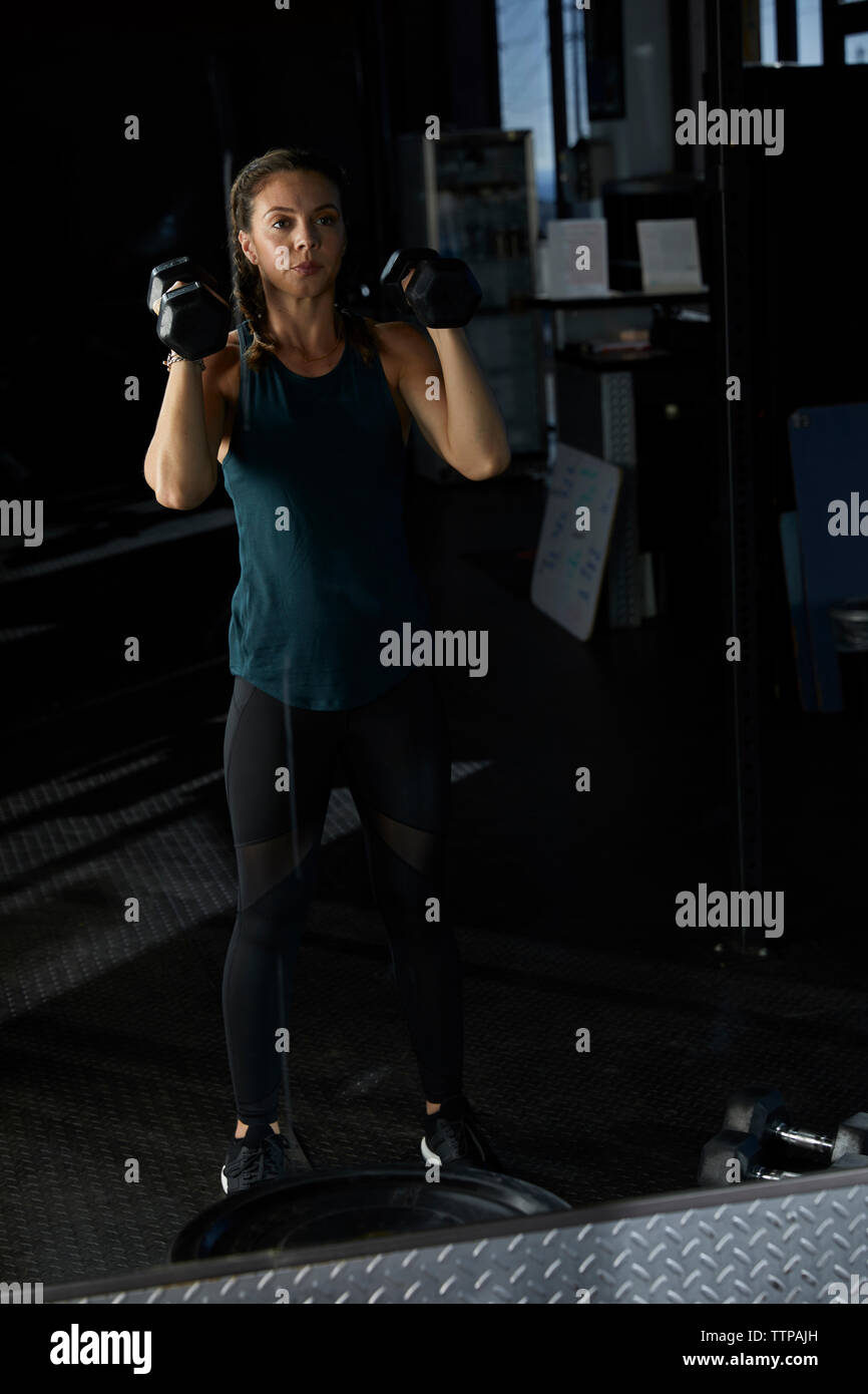 Refection of woman lifting dumbbells while exercising at gym seen in ...