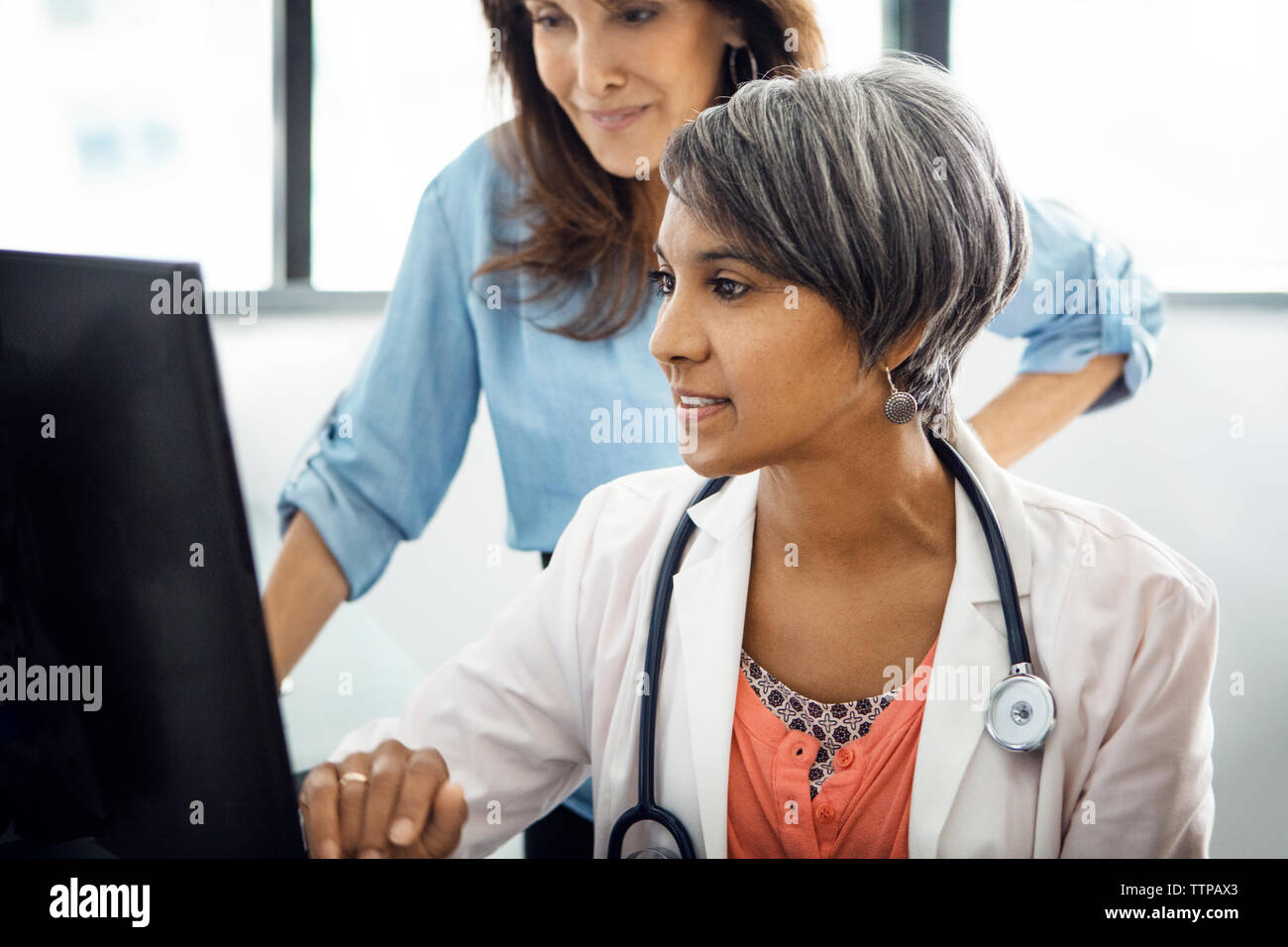 Female doctor using computer with patients in clinic Stock Photo - Alamy