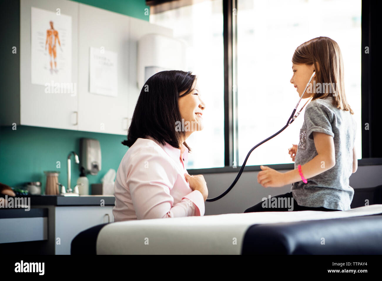 Side View Of Girl Listening To Heartbeat Of Female Doctor Through