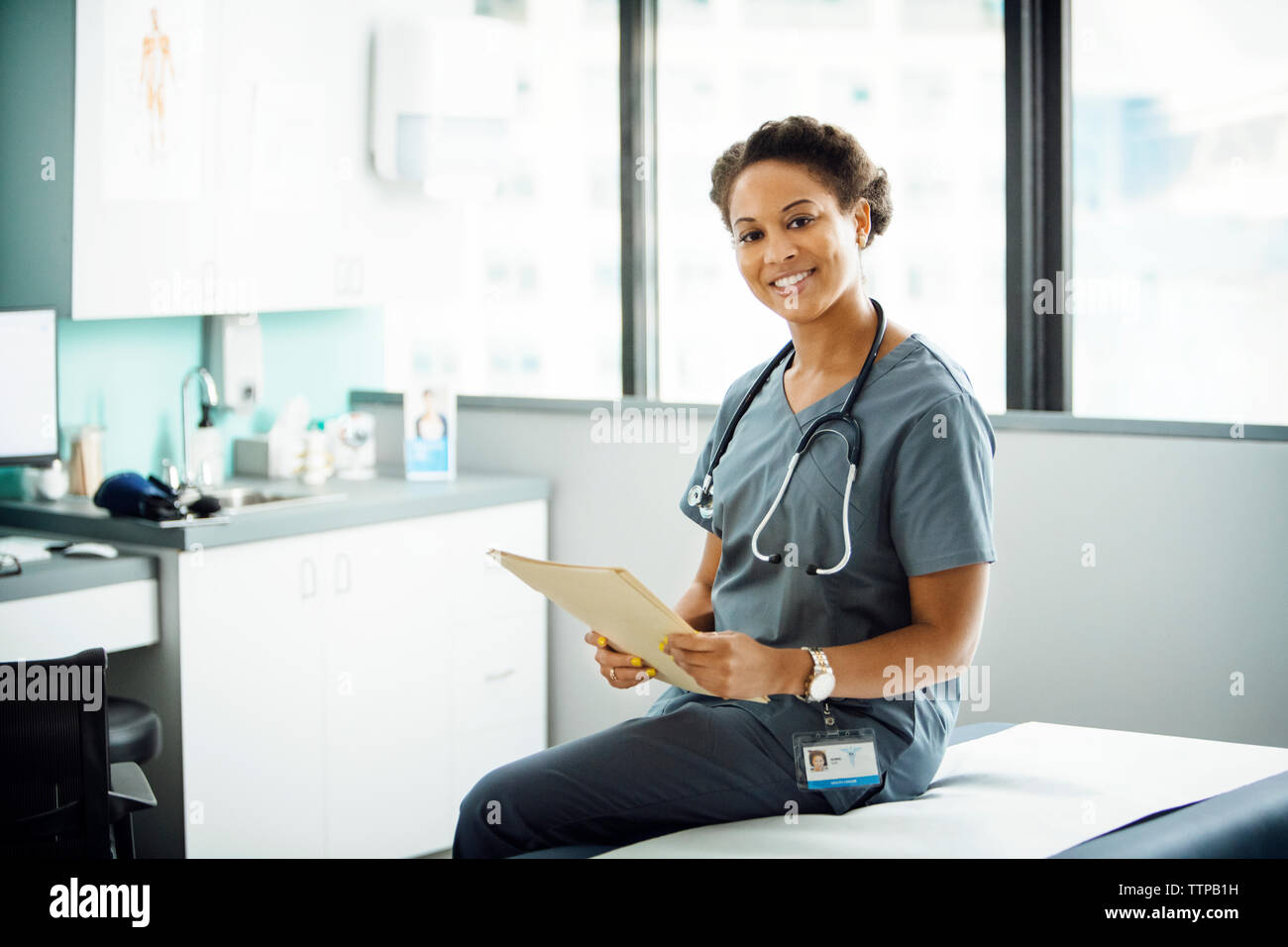 Portrait of happy female doctor holding file while sitting on ...