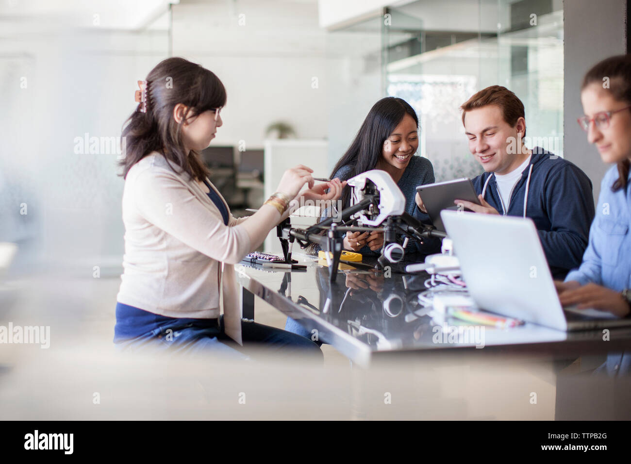 Female student repairing drone by friends using computer at table in ...