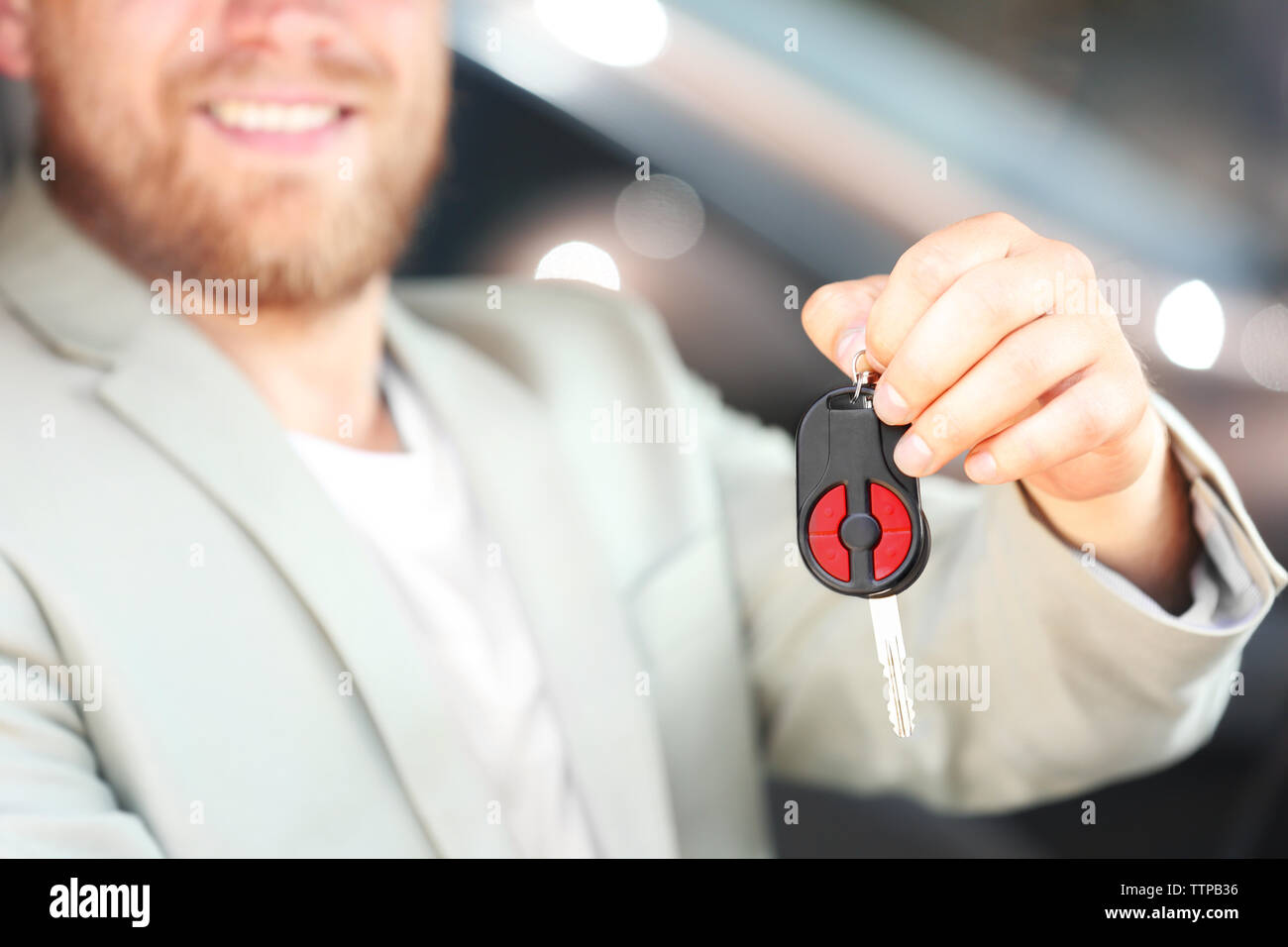Portrait of a successful male dealer showing key while sitting in ...